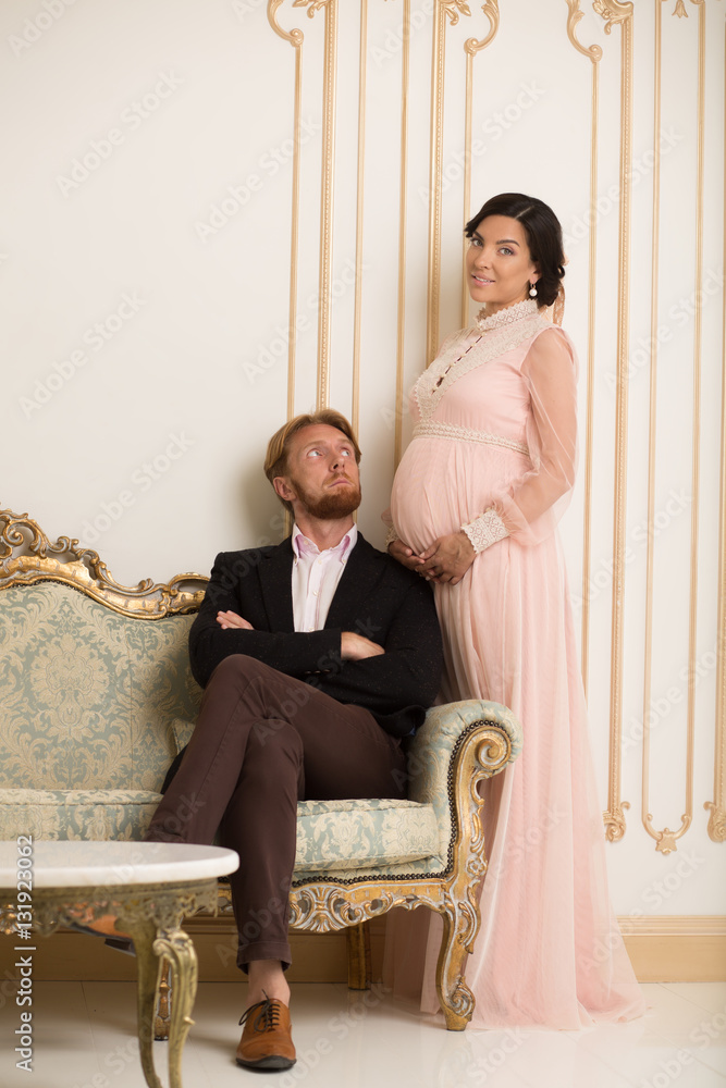 Handsome rich man sitting on sofa and looking at his pregnant wife ...