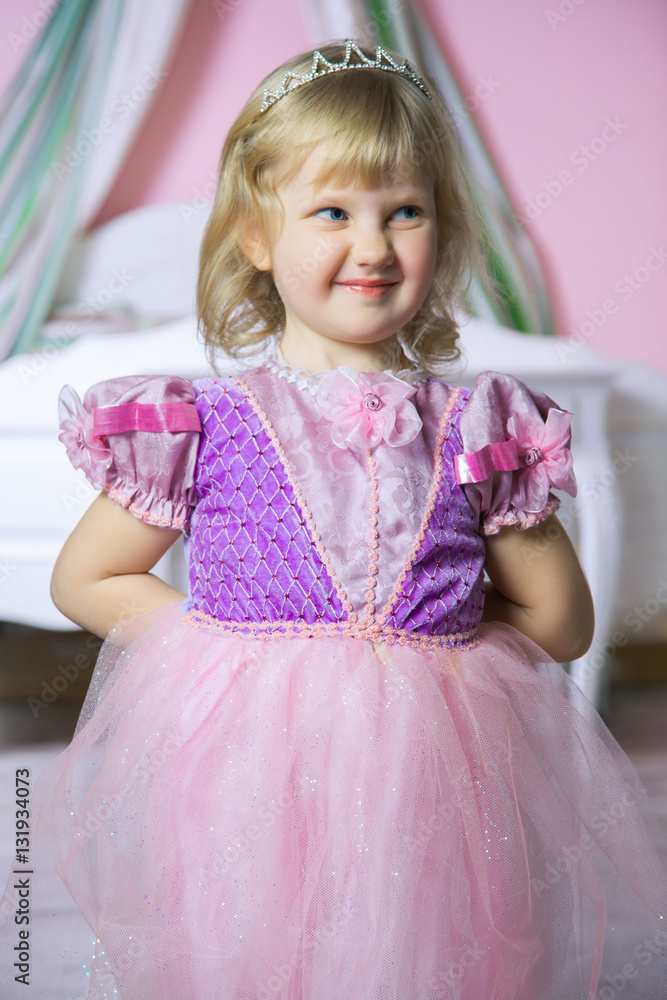 Little happy princess girl in pink dress and crown in her royal room ...