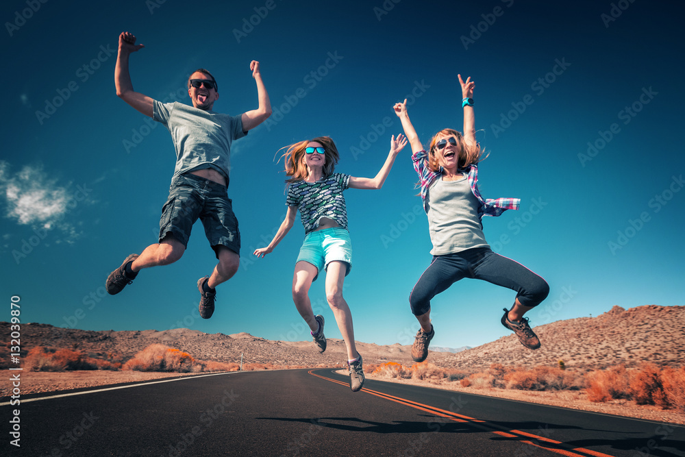 Three young friends jumping and having fun on the empty asphalt road ...