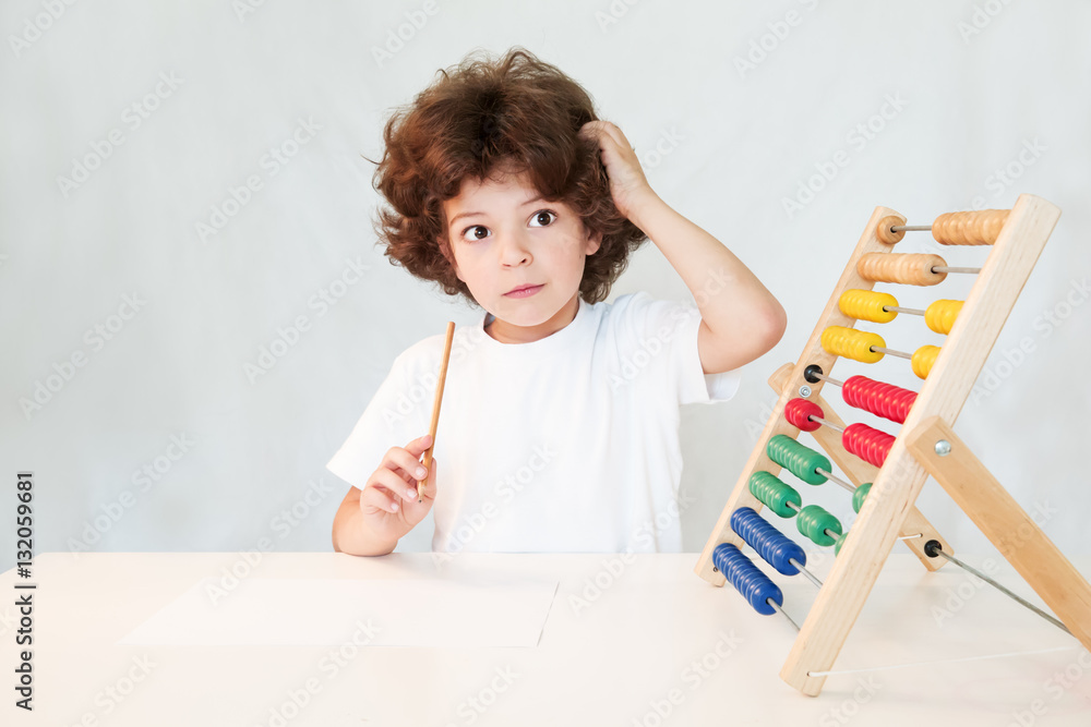 Cute curly-haired boy with a pencil in his hand thoughtfully scratching ...