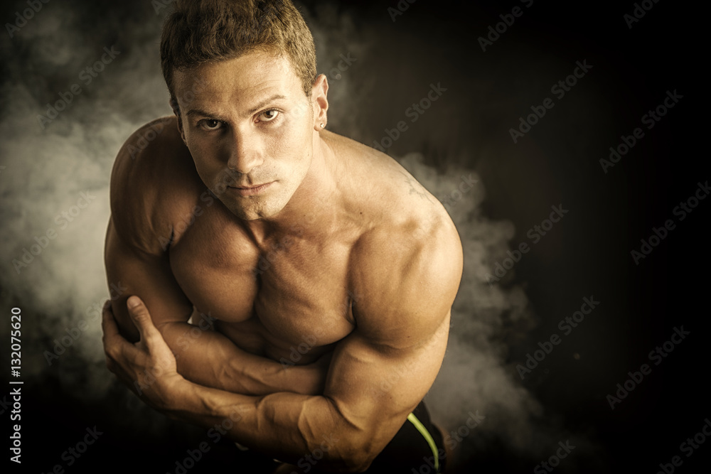 Handsome shirtless bodybuilder shot from above, standing on dark smoky ...