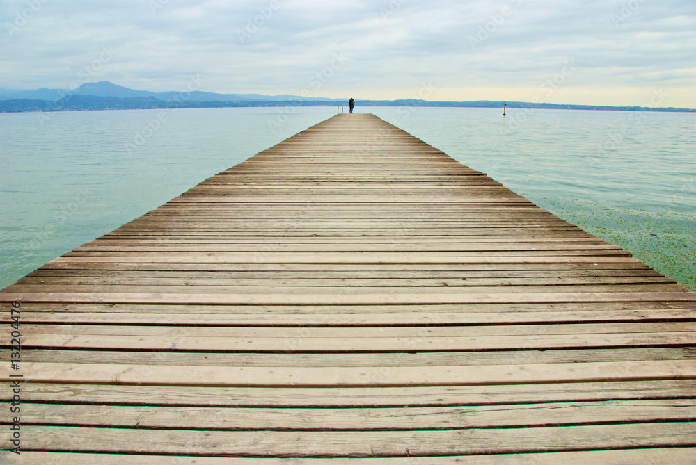 Foto Stock Pontile in legno con persona da sola sullo sfondo | Adobe Stock