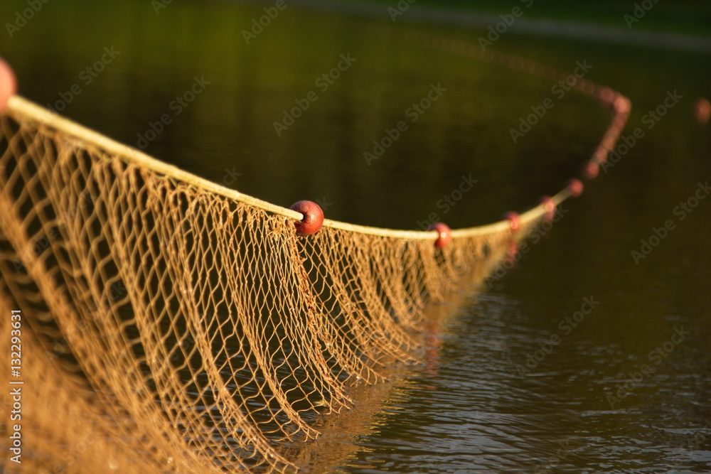 Large sunlit fishing net with red floats cast diagonally across dark ...