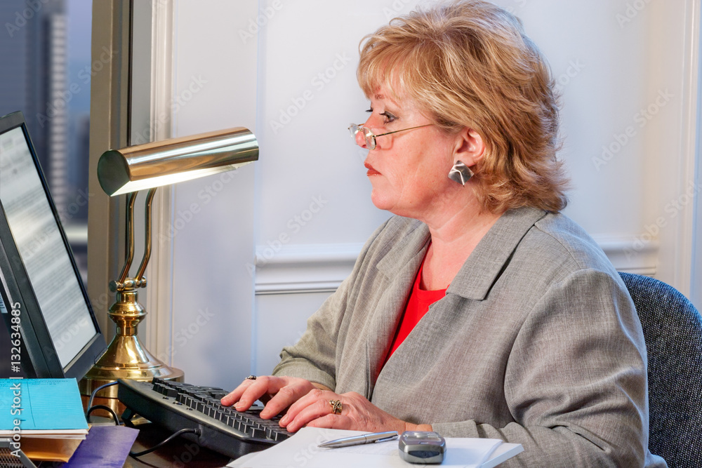 Mature woman peering over her reading glasses as she types Stock Photo ...