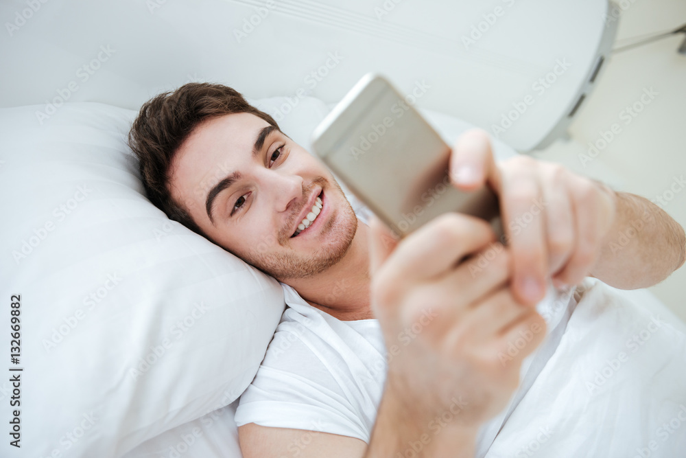 Foto Stock Man lying and using mobile phone in bed | Adobe Stock