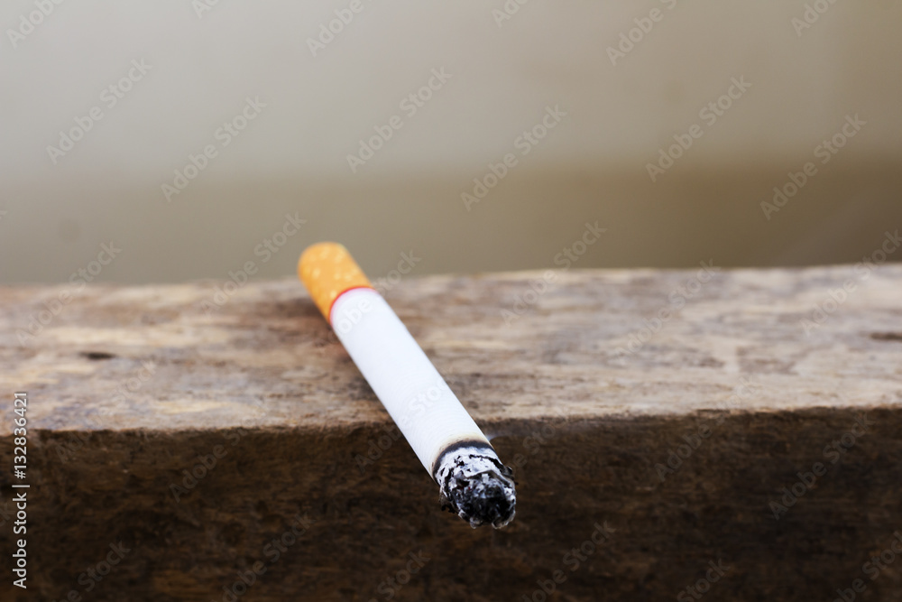 Burning cigarette with ash and smoke on the outdoor wooden table. Bad ...