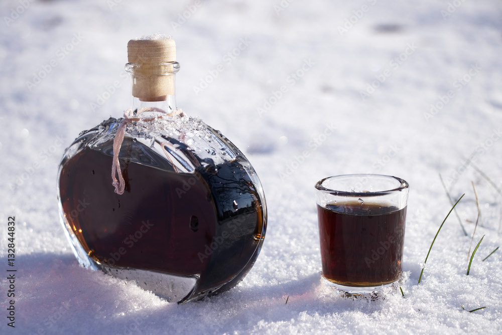 walnut liqueur in the snow. bottle and shot glass in the frosty sunny ...