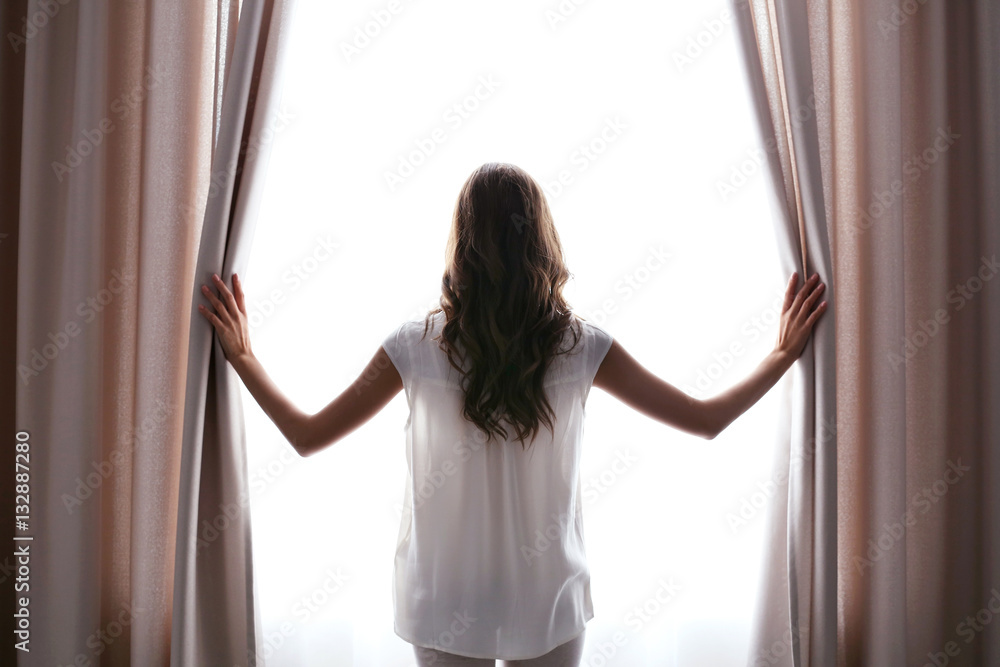 Beautiful woman opening curtains and looking through the window Stock ...