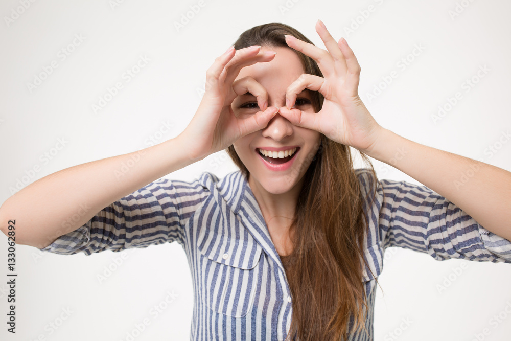 girl making a finger glasses on her face and smiling over white ...
