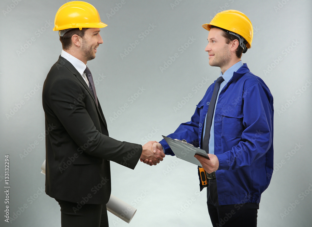 Handsome engineer and worker shaking hands on light background Stock ...