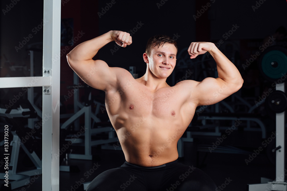 professional fitness bodybuilder sitting on the bench and demonstrates ...
