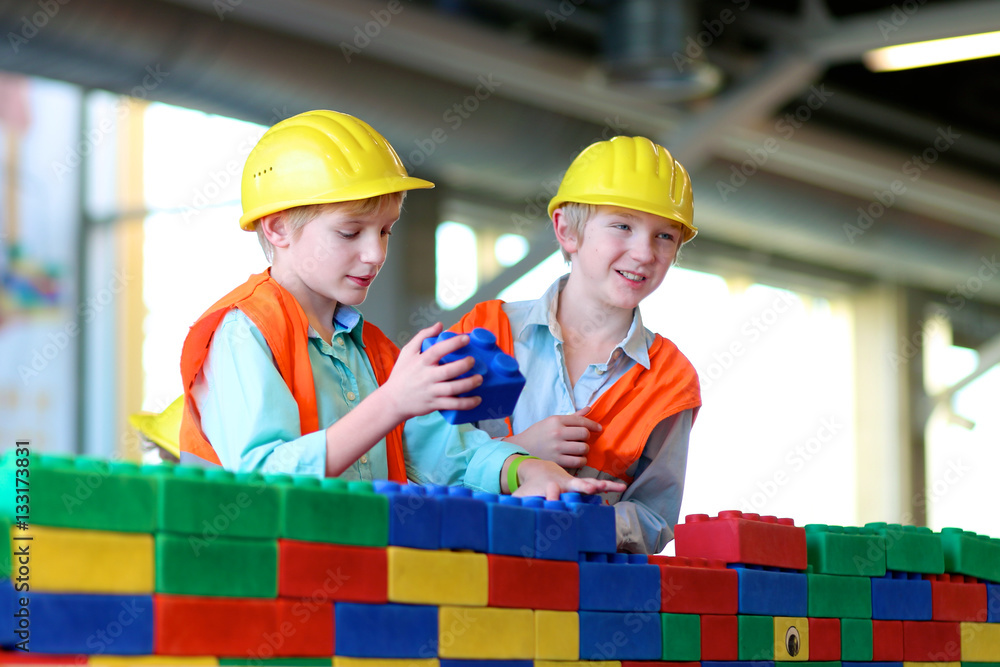 Happy boys in safety helmets playing indoors. Schoolchildren building ...