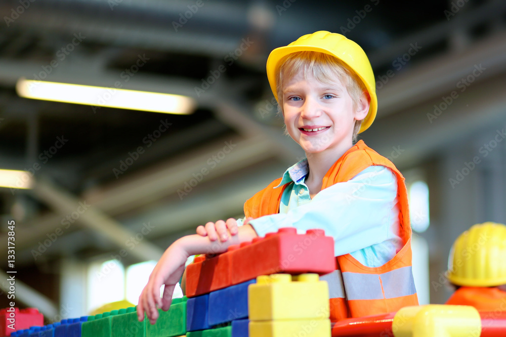 Happy boy in safety helmet plays indoors. Schoolchild building house ...