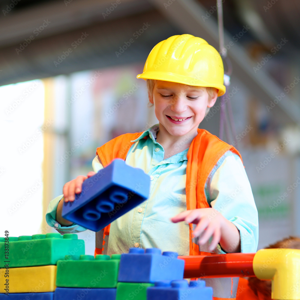 Happy boy in safety helmet plays indoors. Schoolchild building house ...