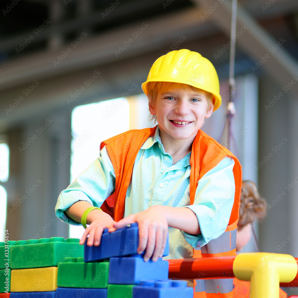 Happy boy in safety helmet plays indoors. Schoolchild building house ...