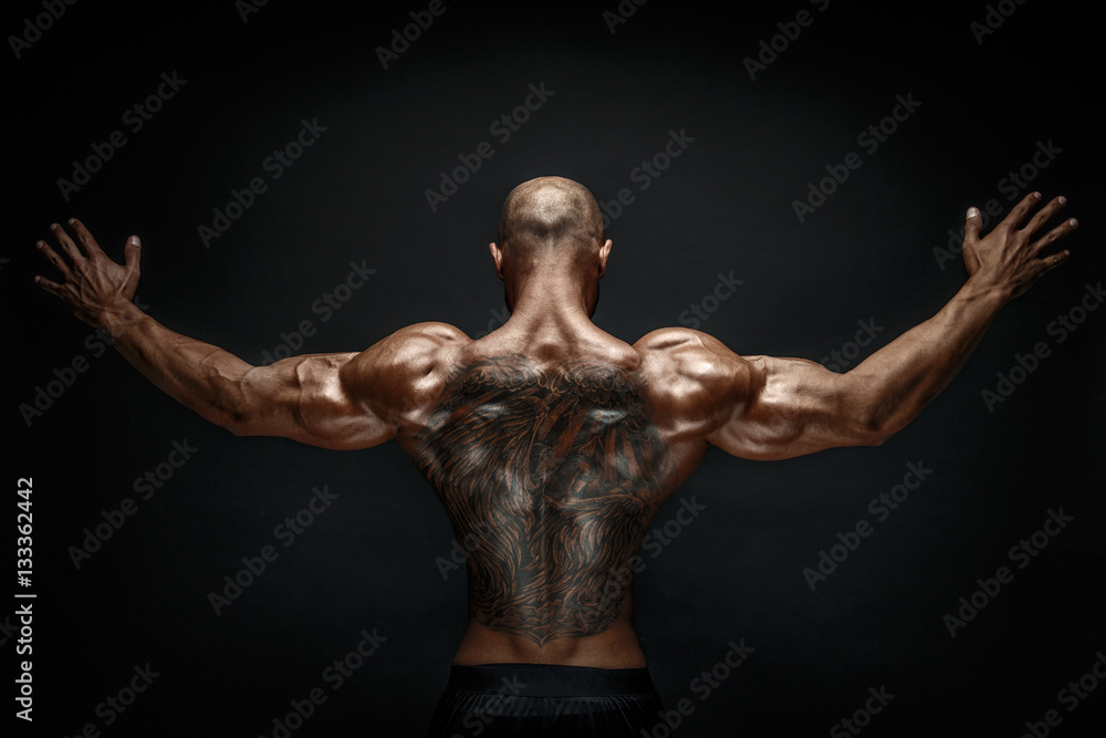 Unrecognizable muscular man with tattoo on back against of black ...
