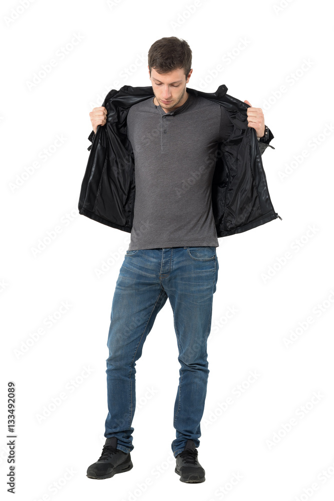 Casual man in jeans taking off leather jacket looking down. Full body ...