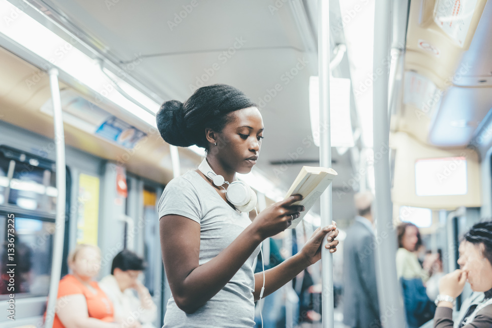 Young beautiful black woman sitting on subway reading a book - commuter ...