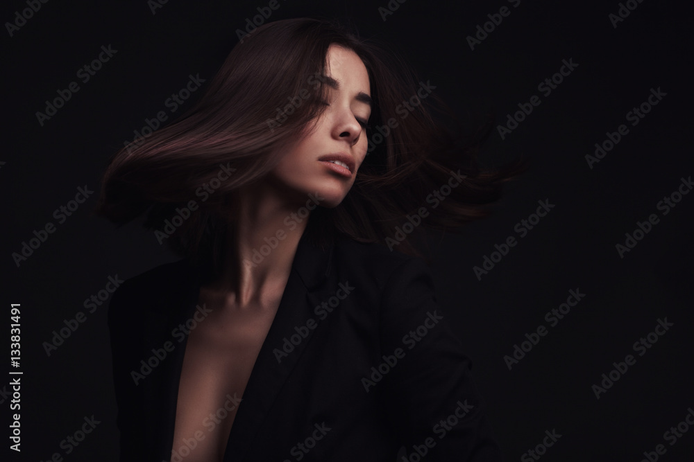 Portrait of a beautiful girl with flying brown hair over dark studio ...