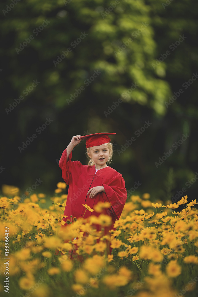 Smiling girl wearing graduation gown standing amidst yellow flowers on ...