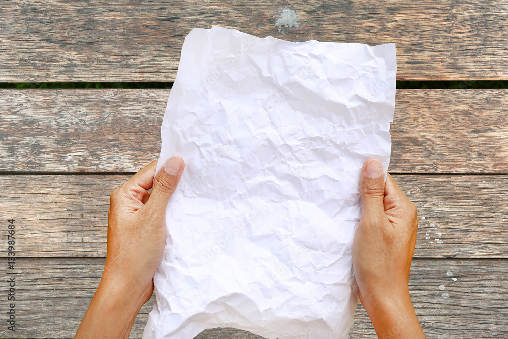 Woman hands holding square crumpled paper against wood plank background ...