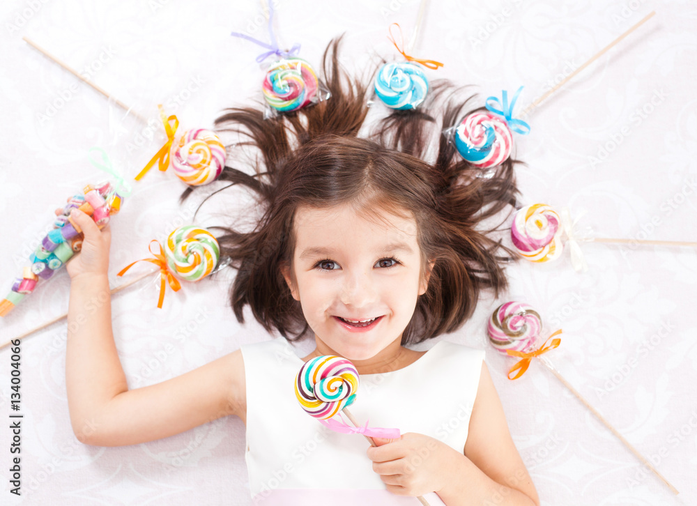 Pretty girl among the sweets, candies and lollipops. Funny child with ...