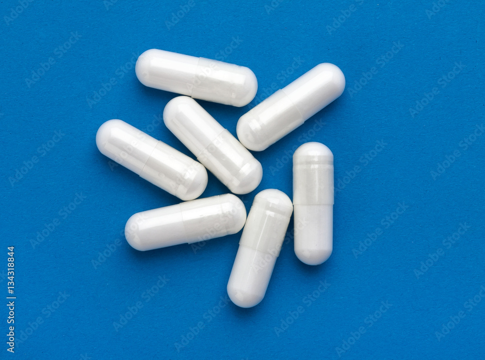 Several white medicine capsules isolated on the blue background. Copy ...