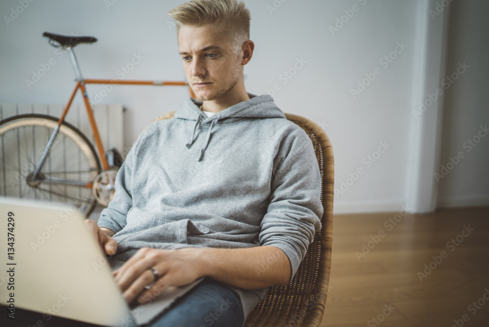 Young hipster man sitting at modern office or coworking space and using ...