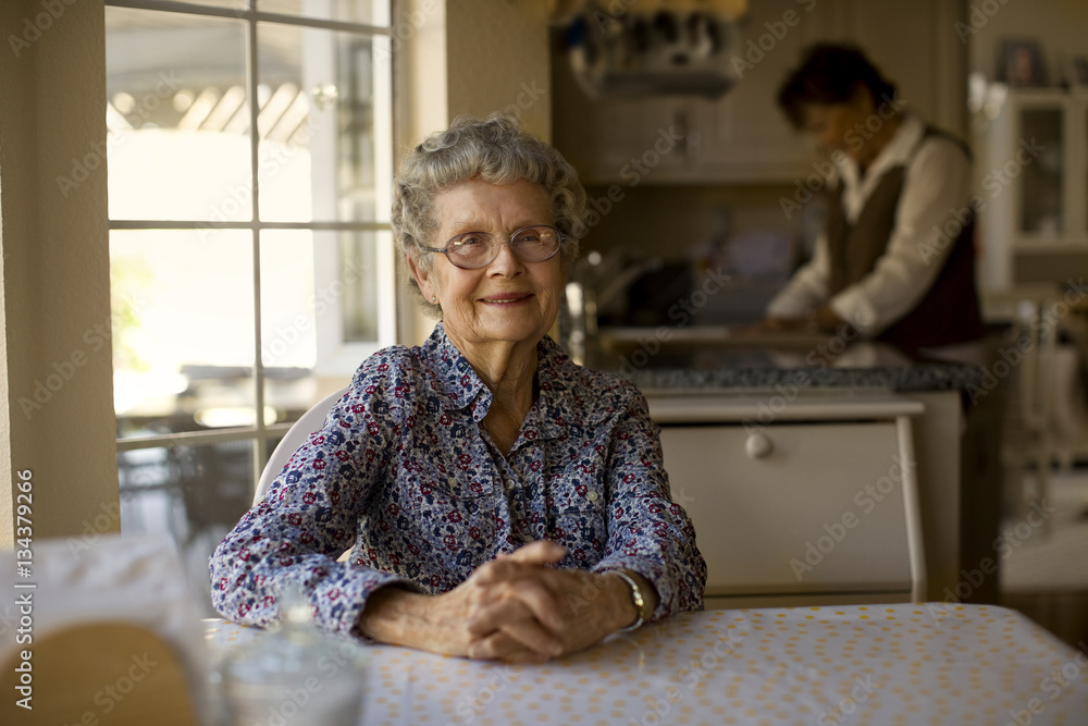 Portrait of a cheerful elderly woman sitting at her kitchen table while ...