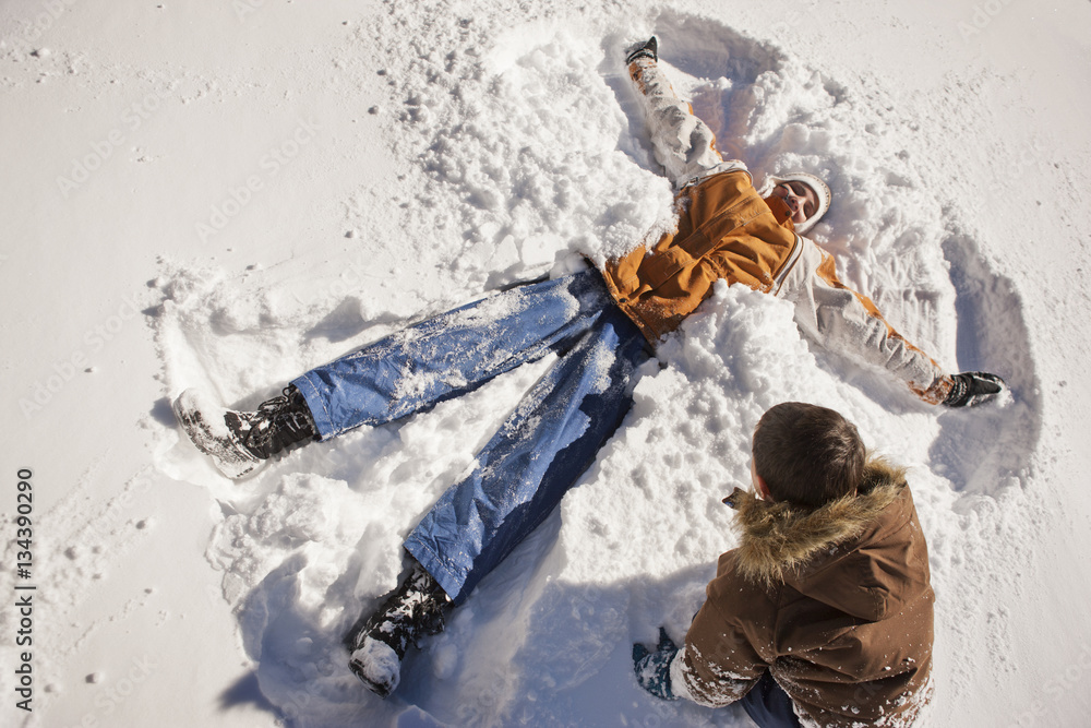 Smiling mid adult woman showing her son how to make a snow angel in the ...