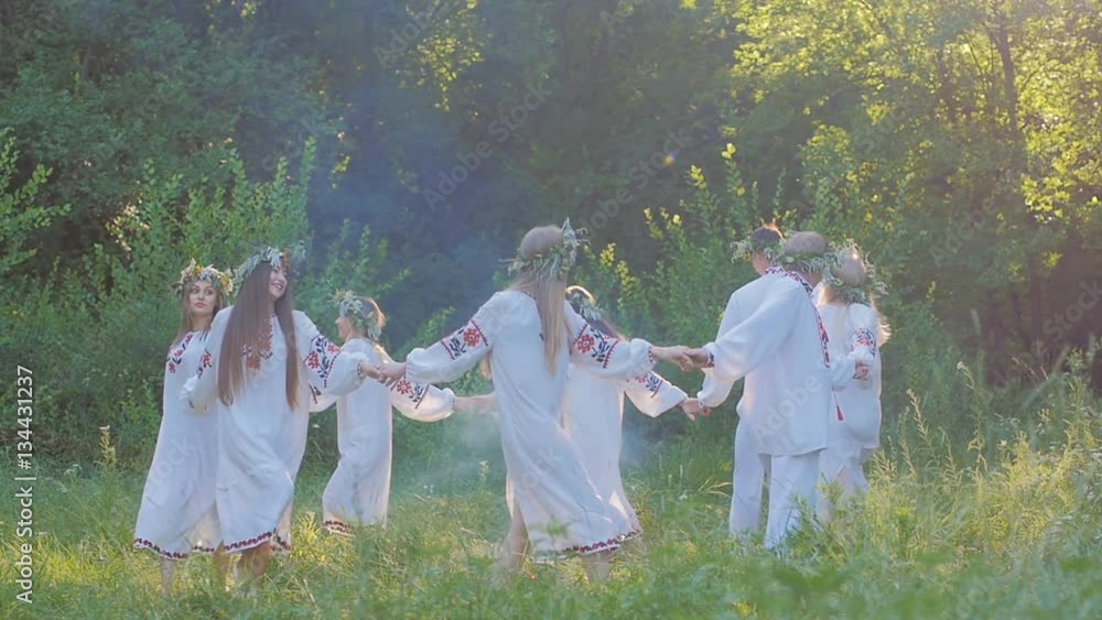 a group of young people in national Slavic costumes dance in a circle around the fire. National ...