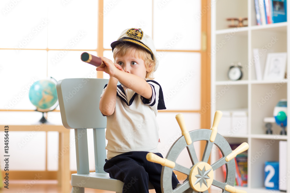 Kid boy dressed like a captain or sailor plays on chair as ship in his ...