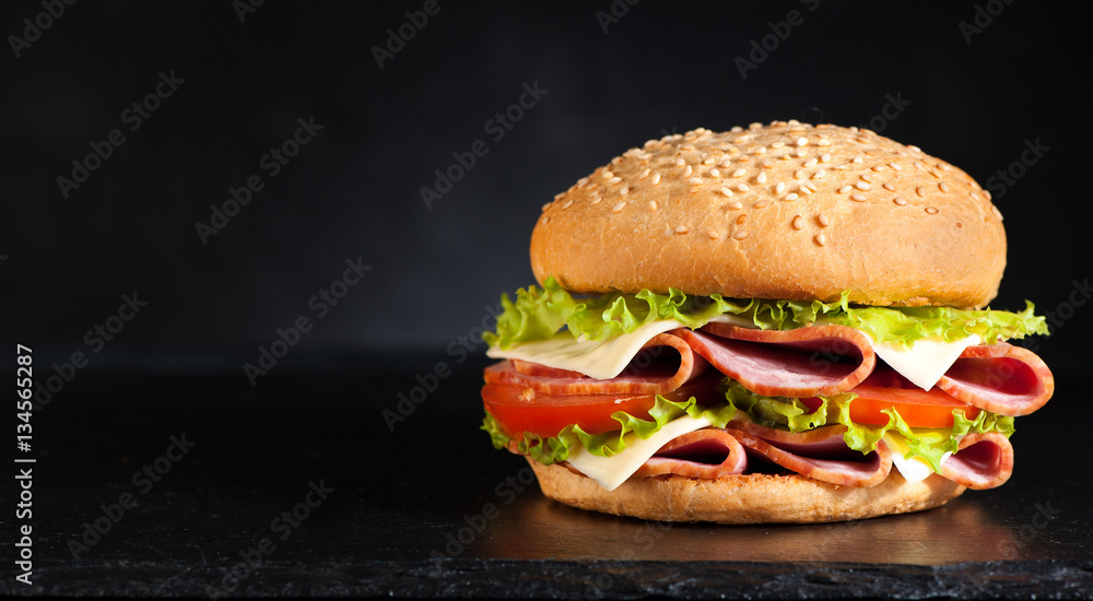 Sandwich burger with ham, cheese and vegetables on a black background ...