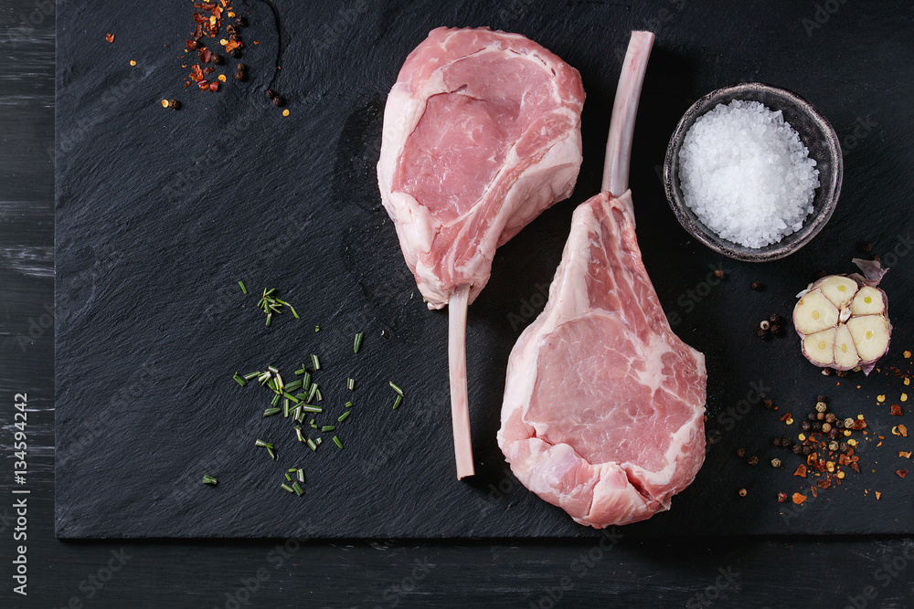 Two raw uncooked Veal tomahawk steak with garlic, salt and seasoning on ...