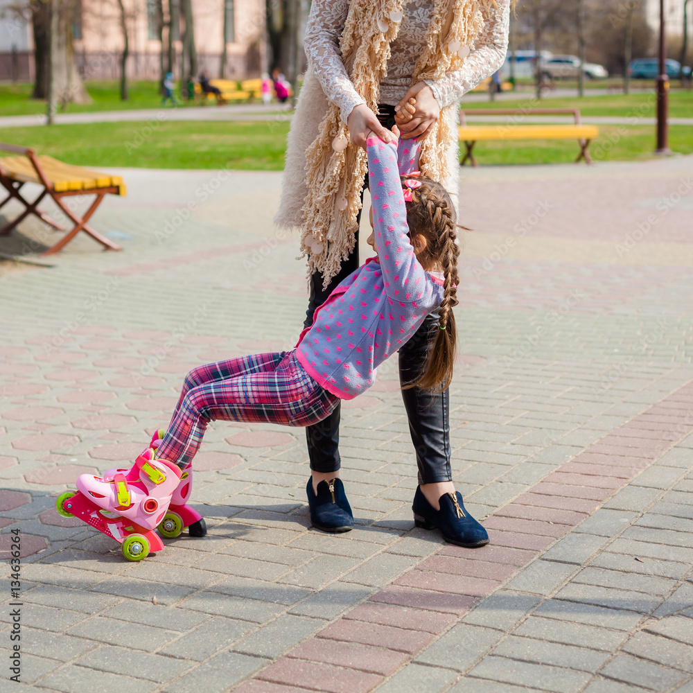 Mom and daughter ride on roller skates. Girl learning to roller skate ...