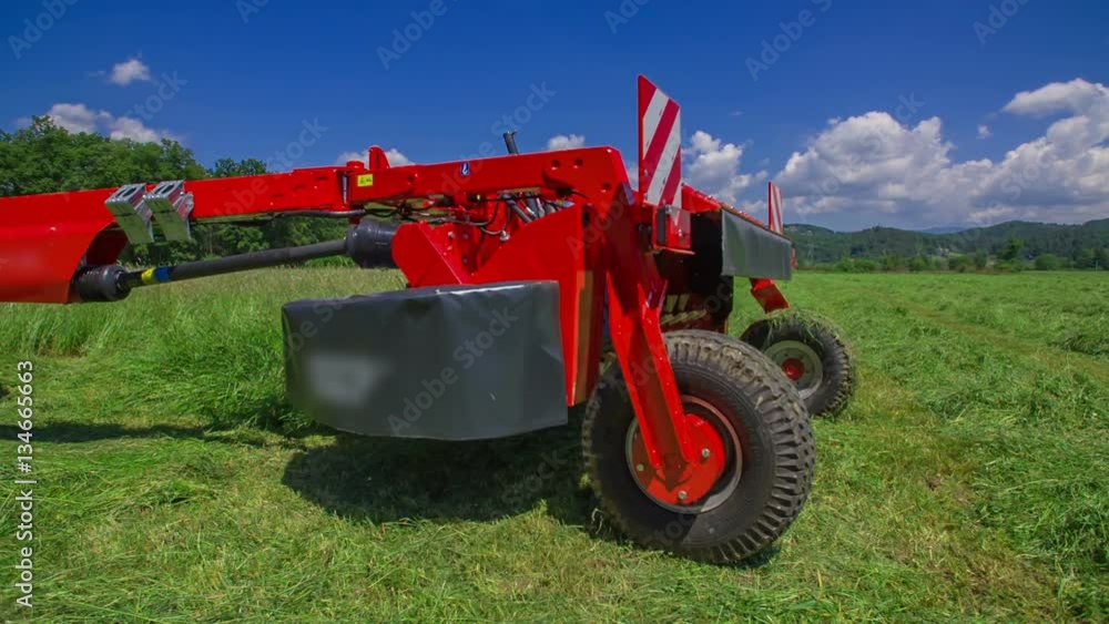 A gras cutting machine lifts up and then down again. A few farmers are ...