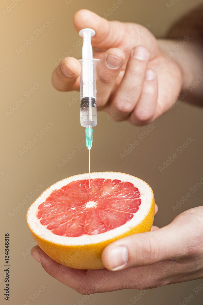 Needle and syringe injected in the fruit. Nutrition concept. Enhanced ...