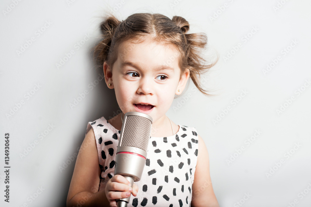 Happy Cute little girl singing a song on microphone. Grey background ...