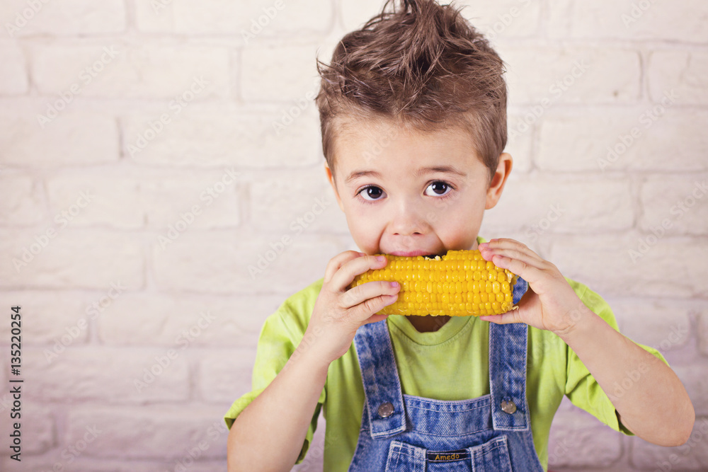 Cute boy eating boiled sweet corn on white bricks wall background Stock ...