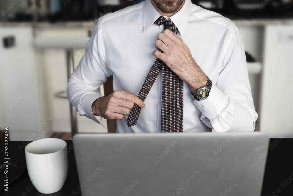 Businessman tying his tie at desk while working from home video chat ...