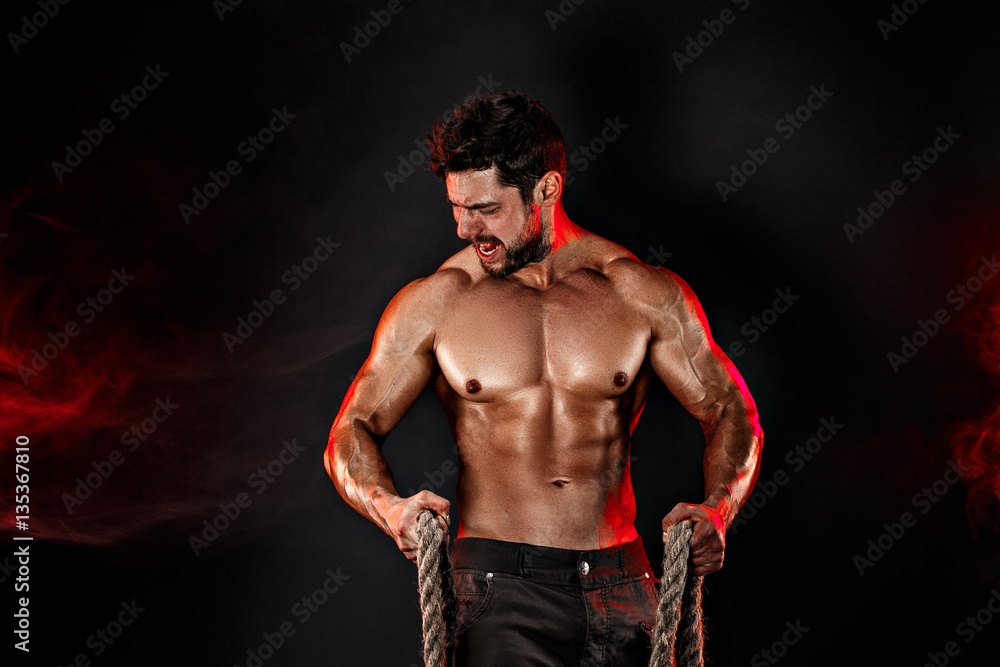 Muscular man holding rope and posing on the black background with red ...