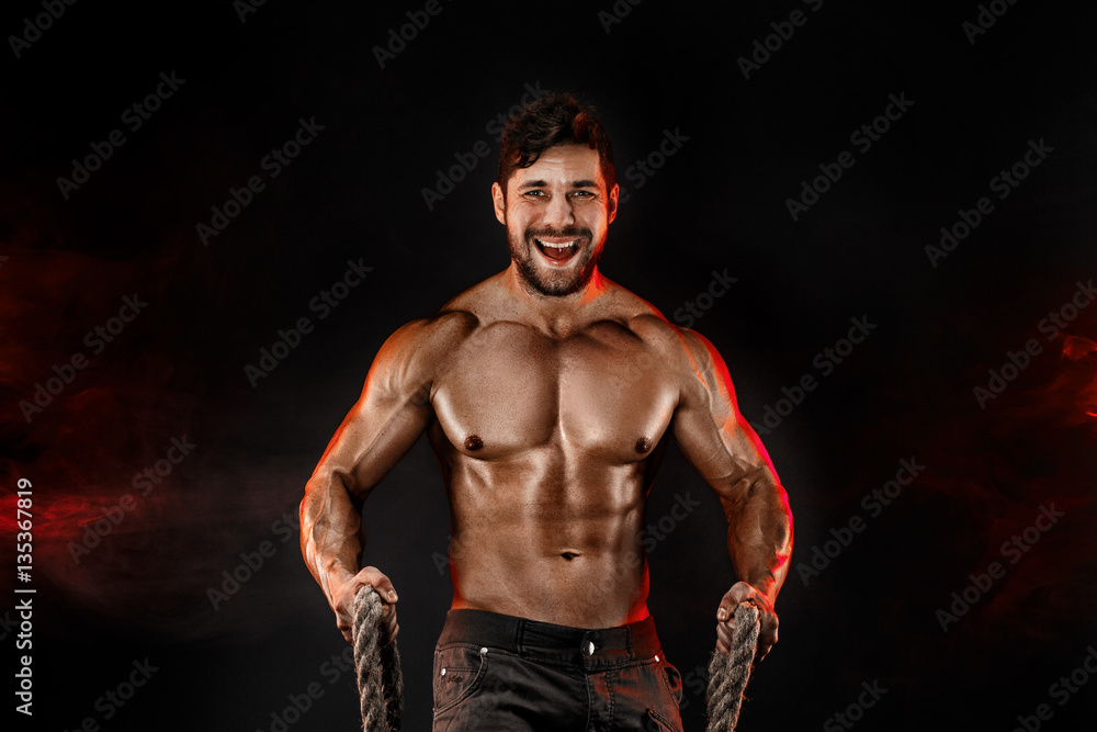 Muscular man holding rope and posing on the black background with red ...