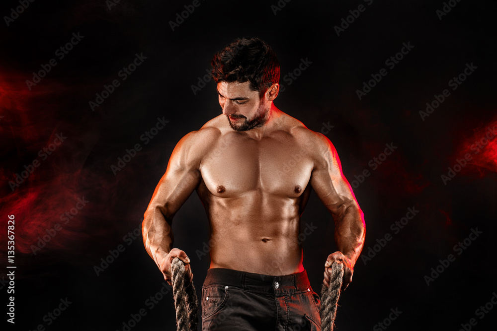 Muscular man holding rope and posing on the black background with red ...