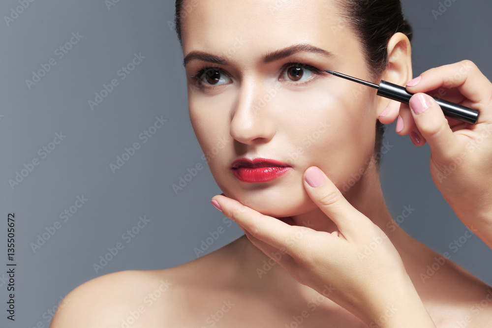 Beautiful girl applying cosmetics on grey background Stock 사진 | Adobe Stock