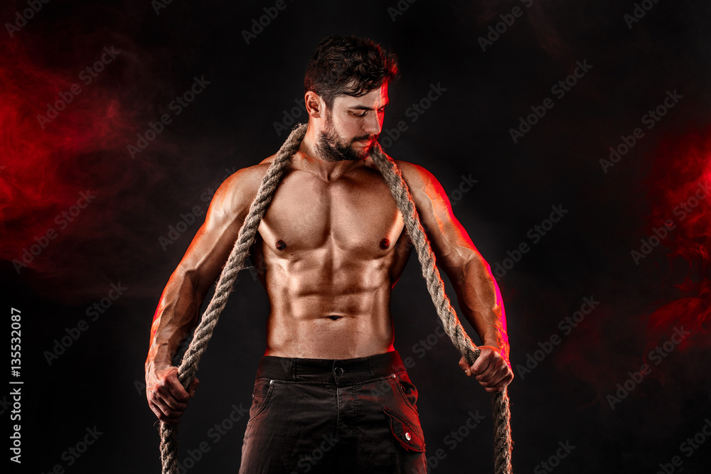 Muscular man holding rope and posing on the black background with red ...