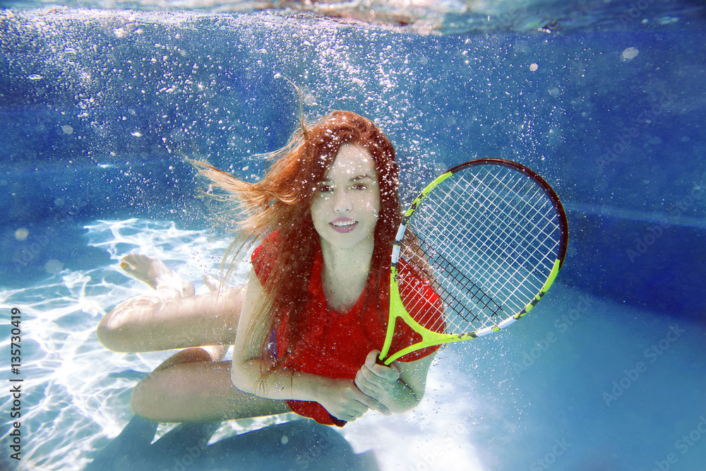 Young beautiful girl playing tennis underwater in the swimming pool ...