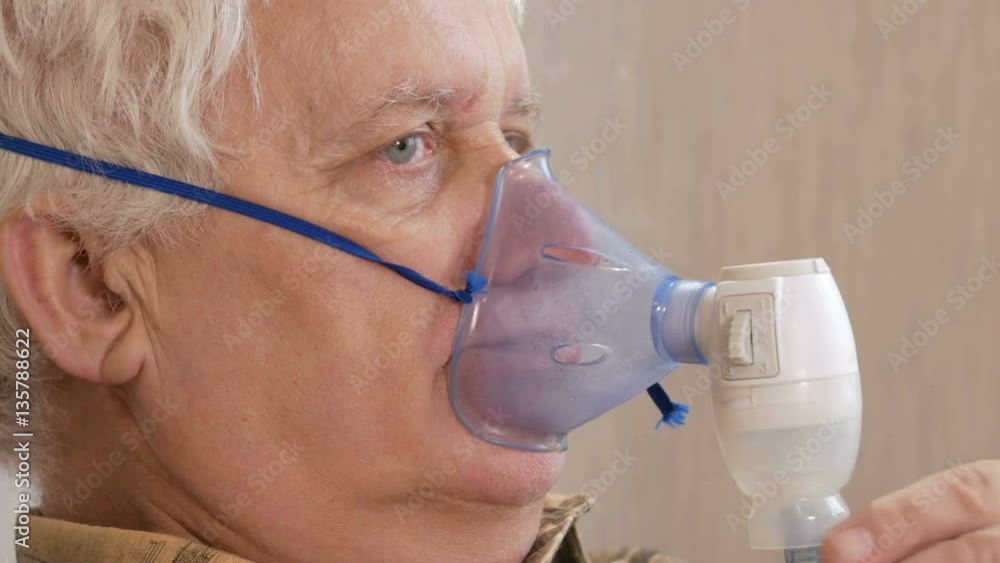 An elderly man holding a mask from an inhaler at home. Treats ...