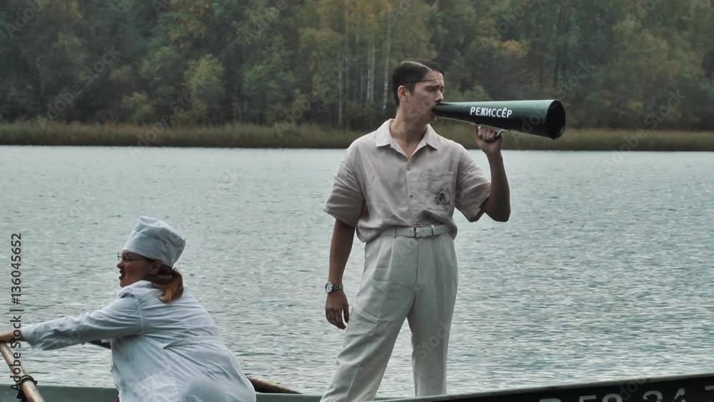 Nurse paddling boat on lake, man in hair net yelling into megaphone ...