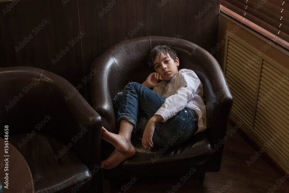 Boy in white shirt sitting in a chair. young boy imposingly placed in a ...