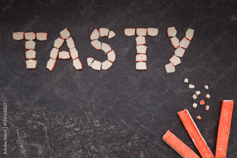 Word tasty created from crab sticks on the dark table in the kitchen ...